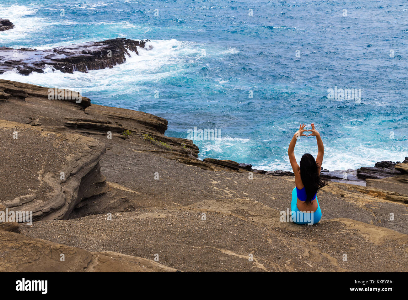Young woman doing yoga exercises, Oahu, Hawaii as she sits on a rocky ...