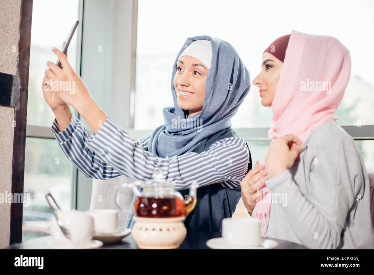 two happy young muslim woman take self portrait with handphone at cafe ...