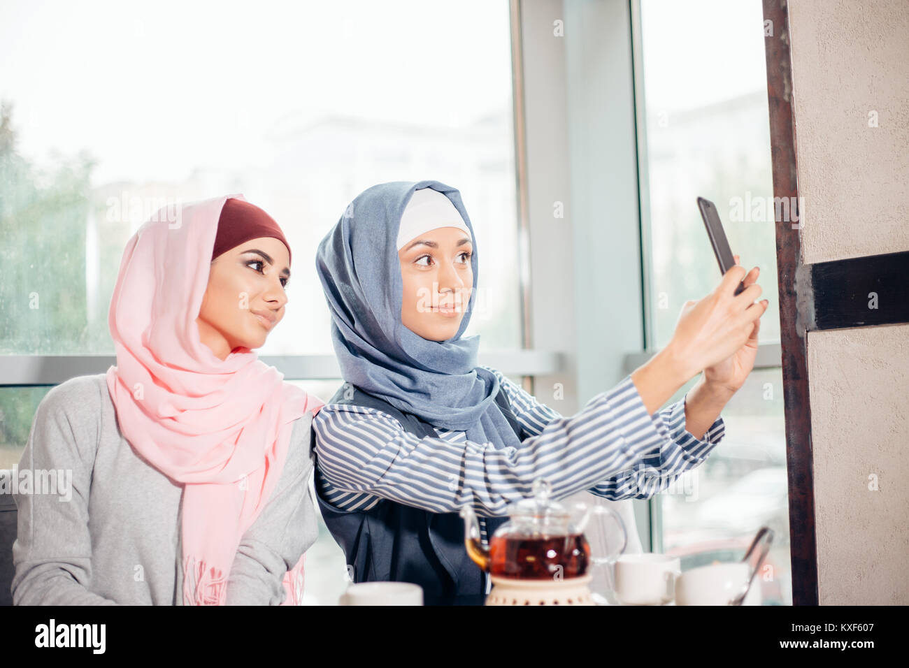 two happy young muslim woman take self portrait with handphone at cafe ...