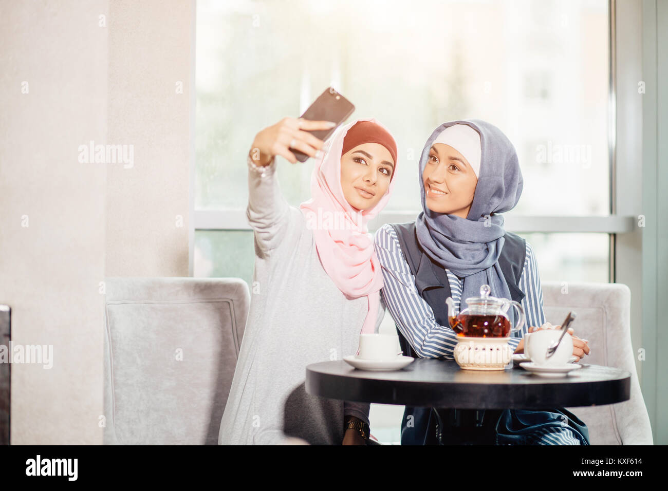 two happy young muslim woman take self portrait with handphone at cafe ...