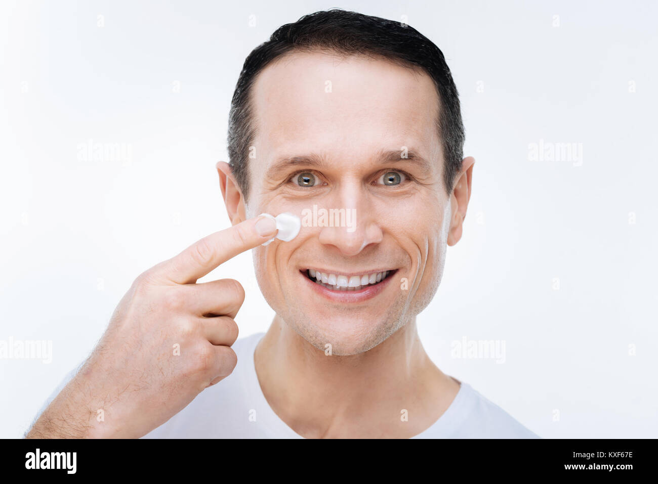 Joyful nice man putting cream on his face Stock Photo - Alamy