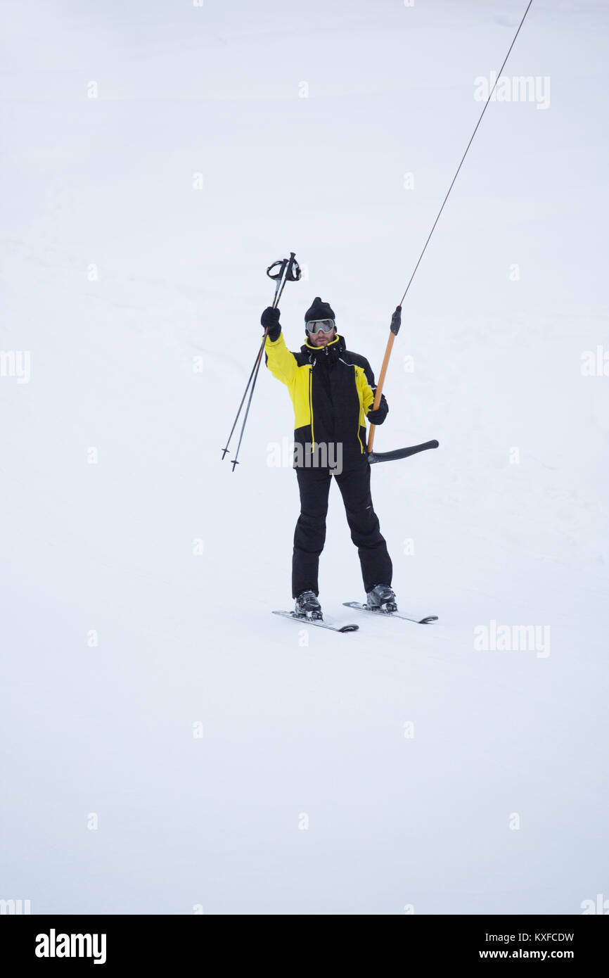 Happy smiling male skier using t bar ski drag lift and greeting waving ...