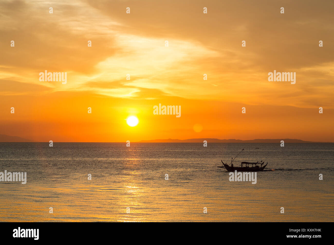 An exotic bangka dive boat motors under a saturated sunset sky in ...