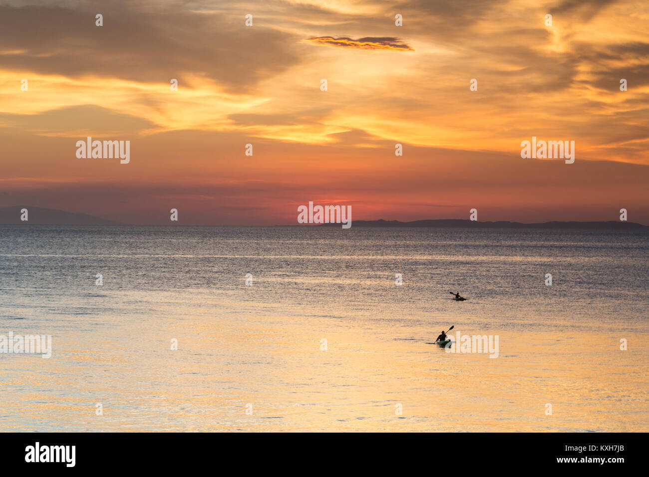 Kayakers paddle across the calm sea under a saturated sunset sky in ...