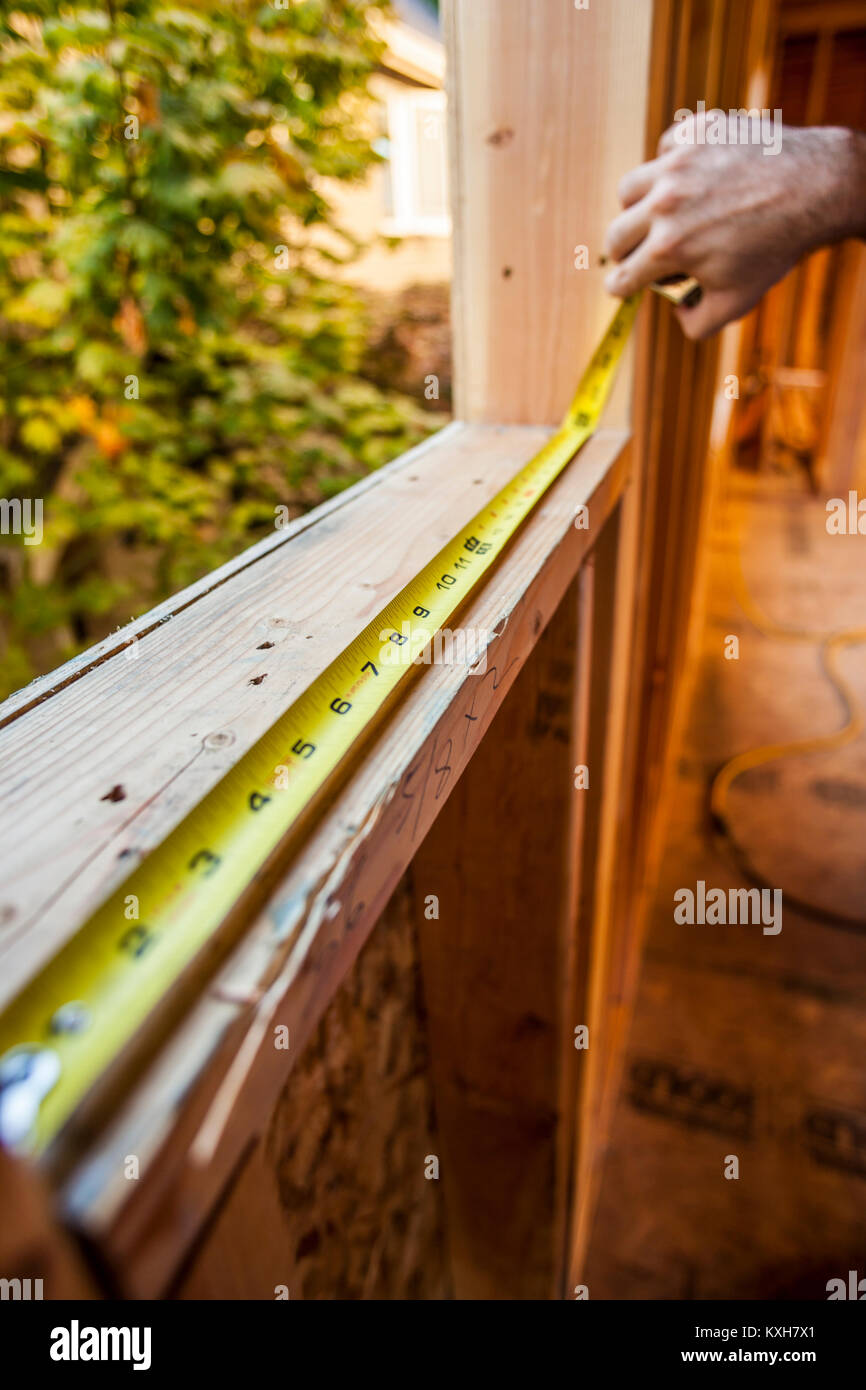 A mans hands measuring a window opening in a house under construction ...