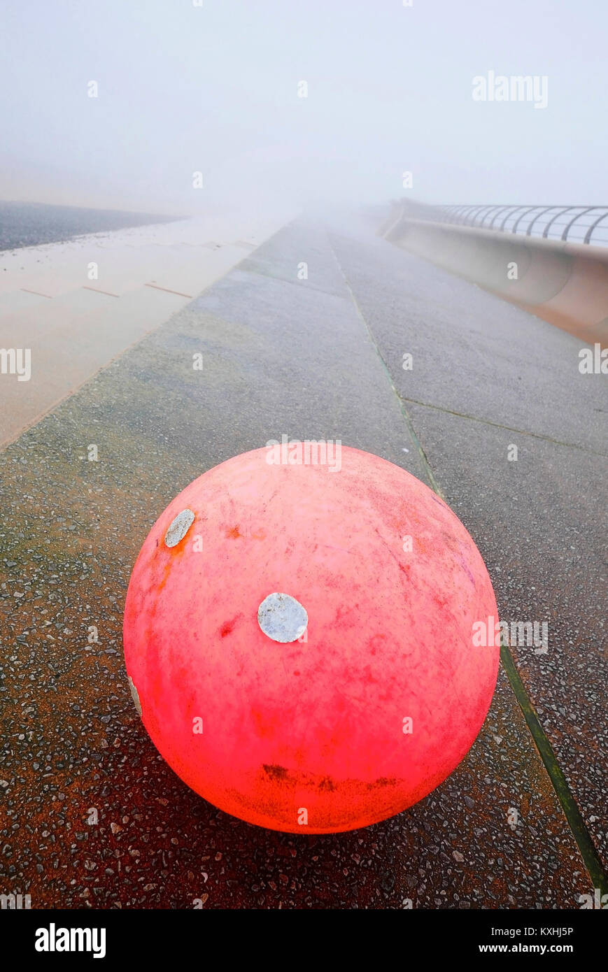 Day glow red boat float washed ashore on to concrete seafront Stock ...
