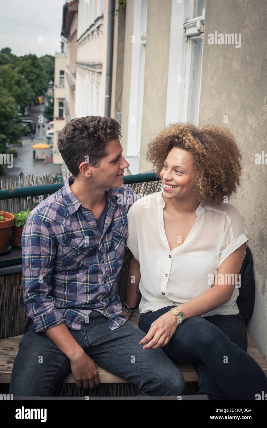 Smiling friends talking while sitting by wall in balcony Stock Photo ...