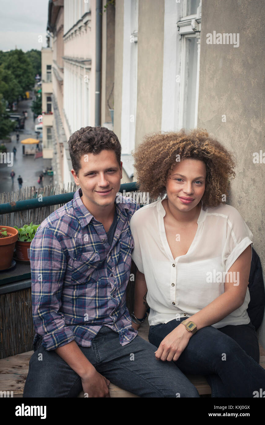 Portrait of smiling young friends sitting by wall in balcony Stock ...