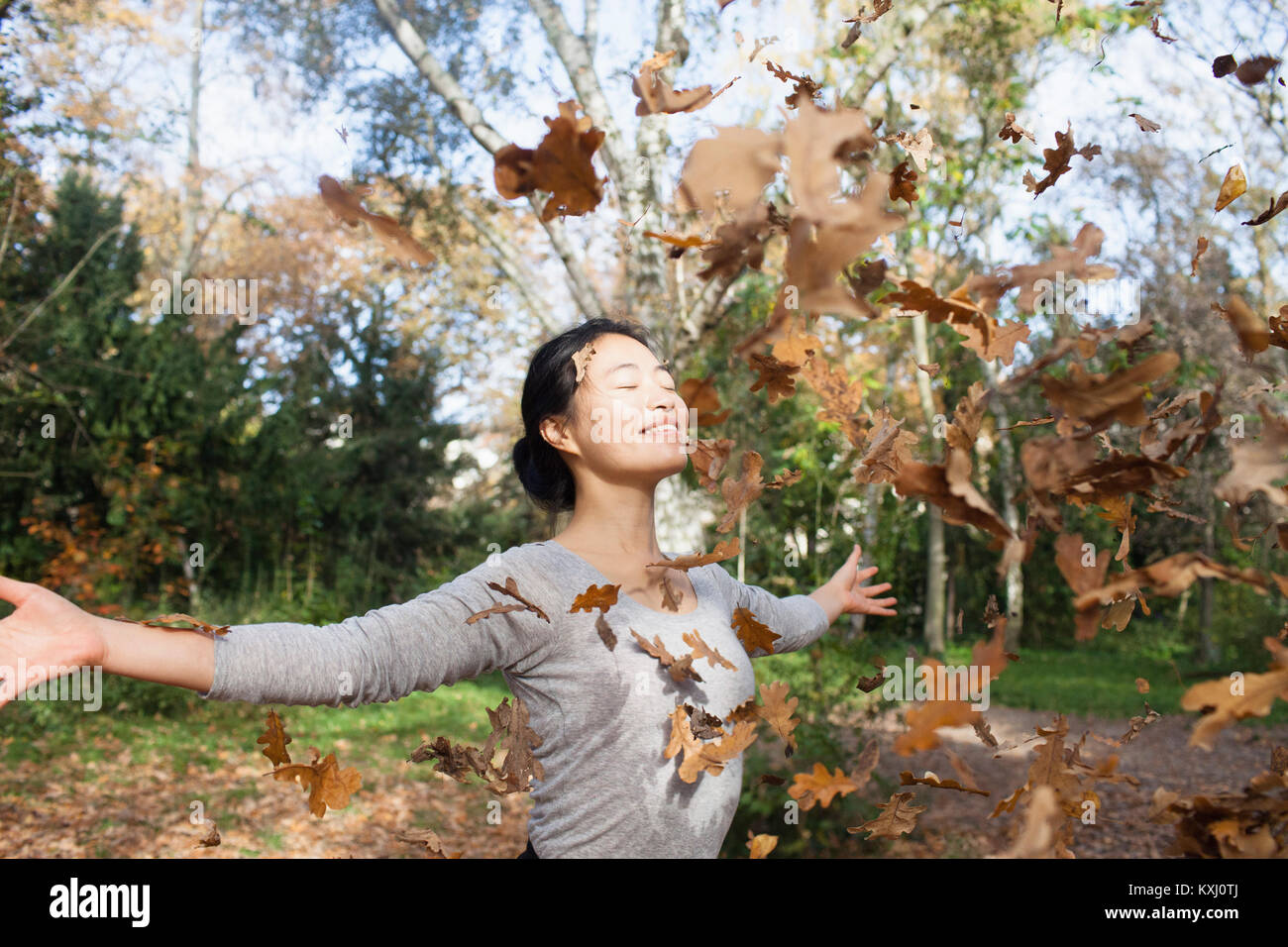 Dry leaves falling on happy woman standing with arms outstretched at ...