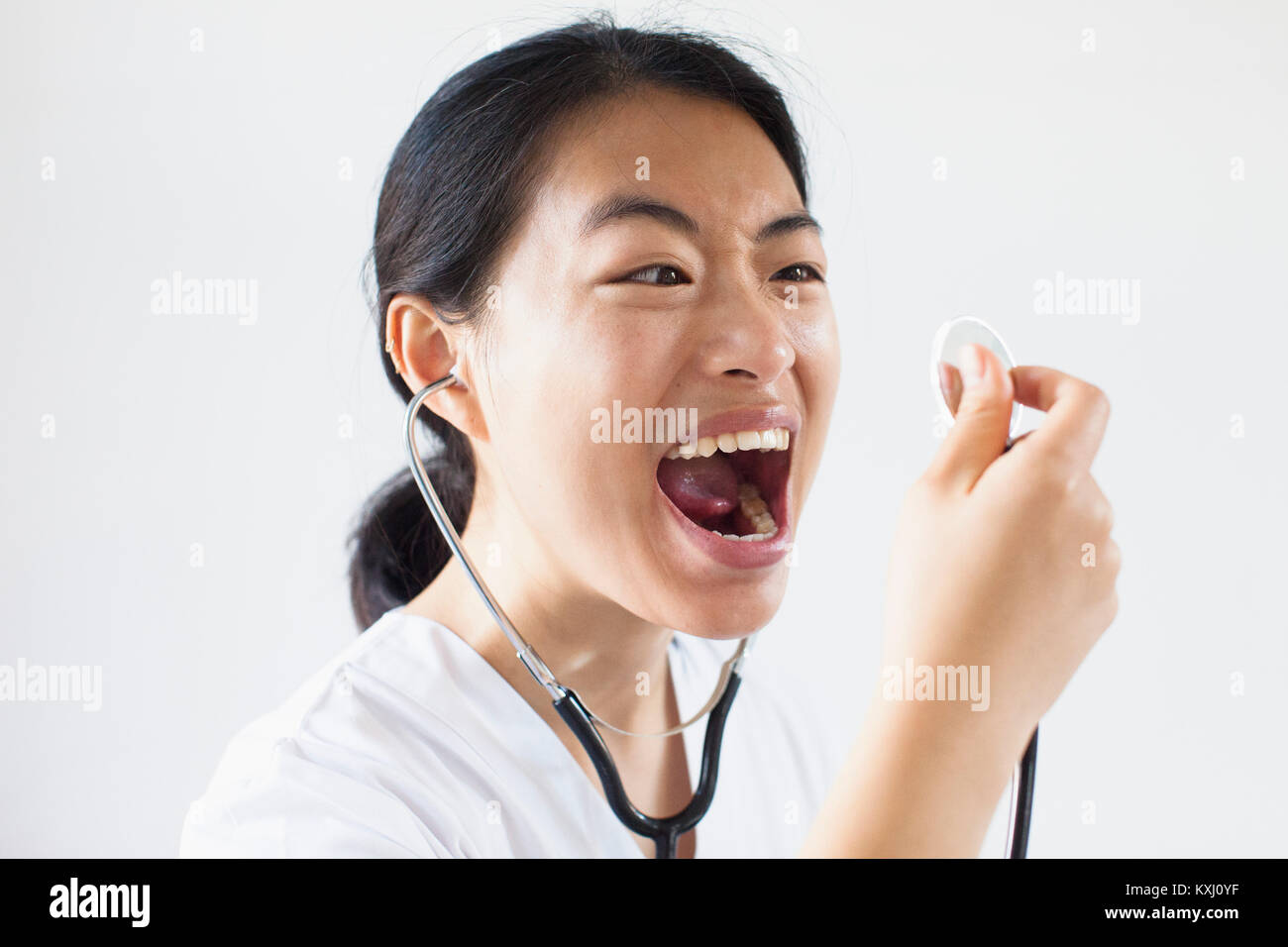 Frustrated doctor screaming with mouth open into stethoscope against ...
