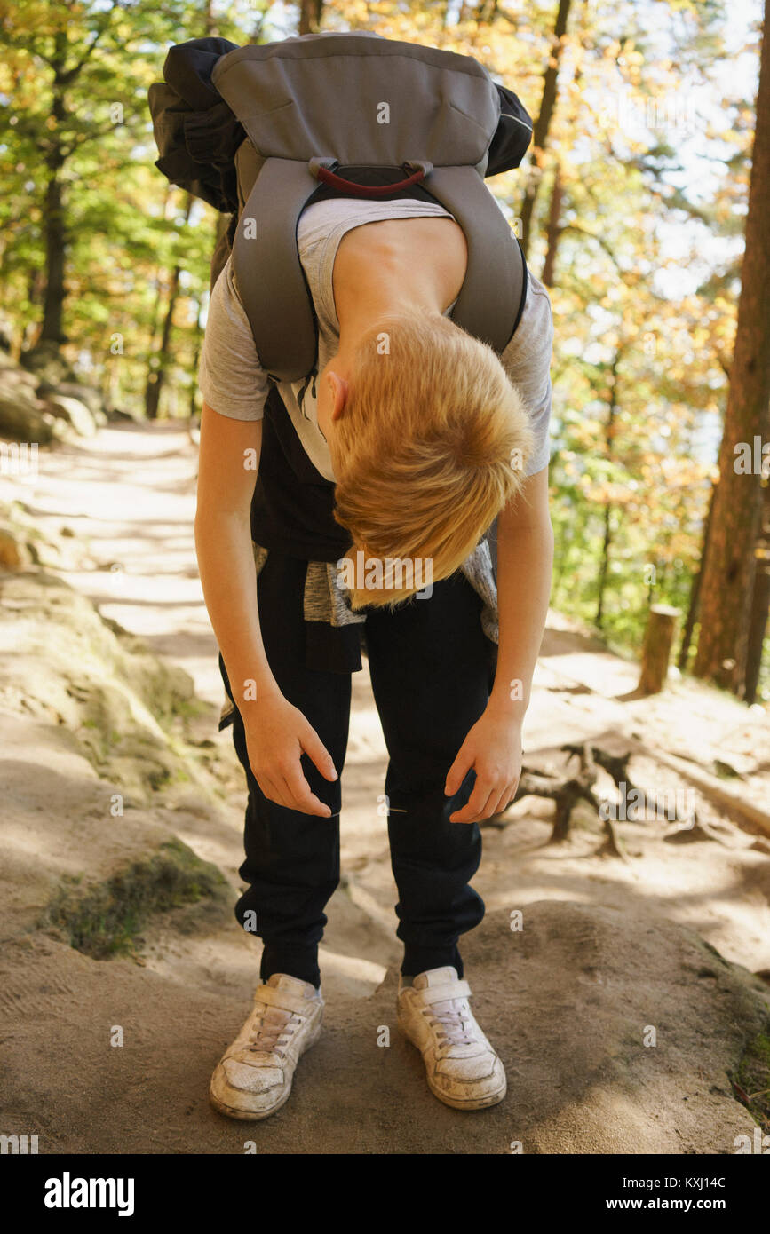 Full length of tired boy with backpack bending against trees in forest ...
