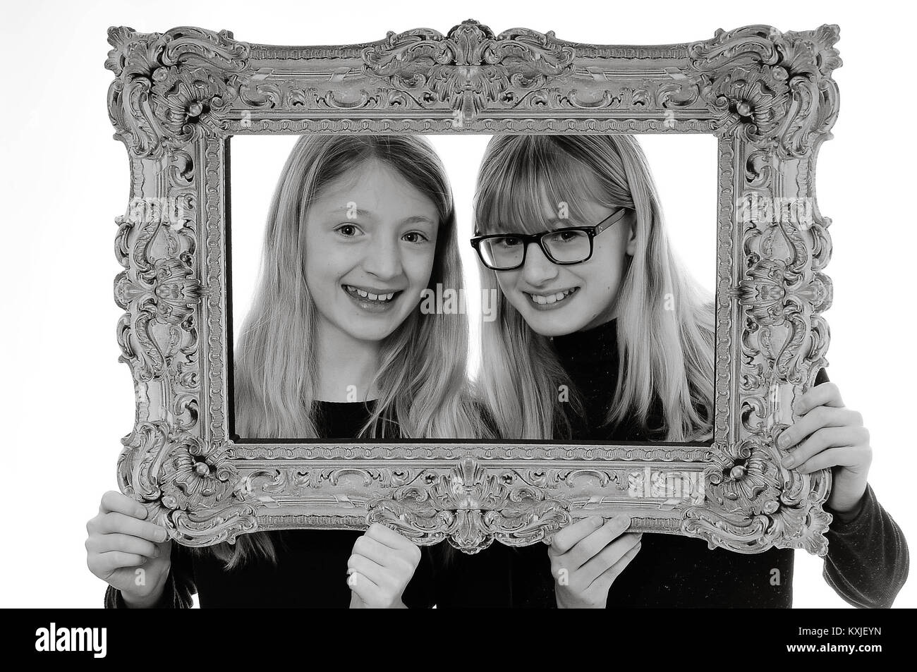 two pretty blonde Caucasian girls, looking through a frame, isolated on ...