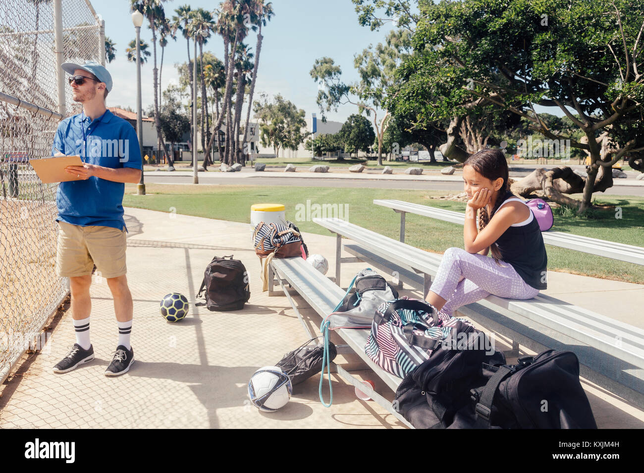 Schoolgirl soccer player alone on bench while teacher watches over ...