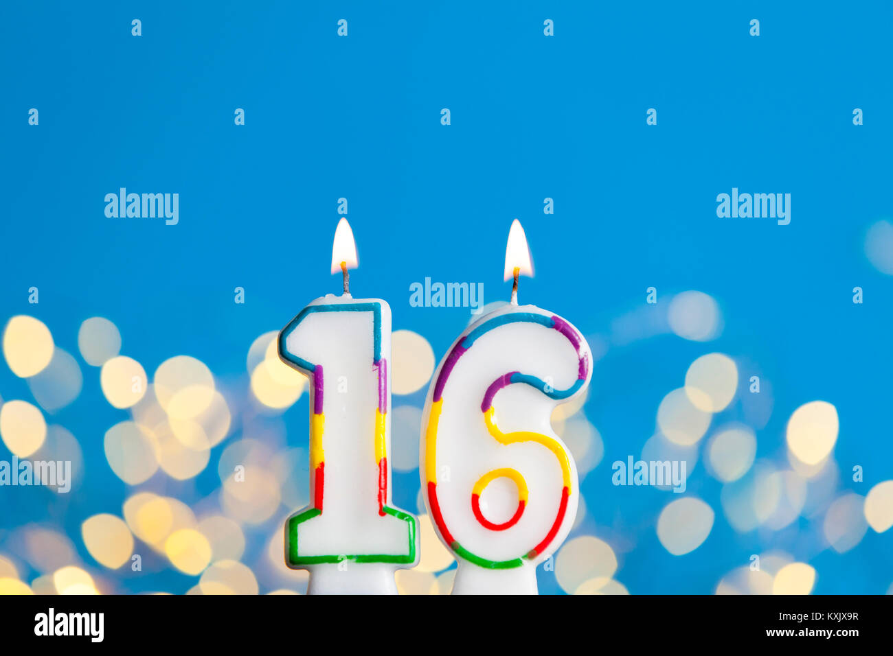 Number 16 birthday celebration candle against a bright lights and blue ...