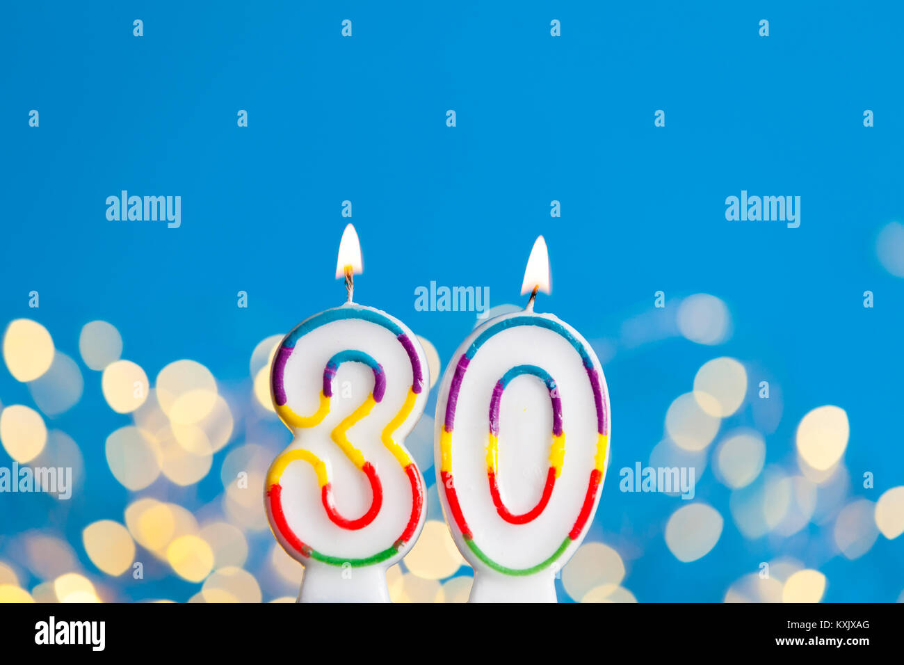 Number 30 birthday celebration candle against a bright lights and blue ...