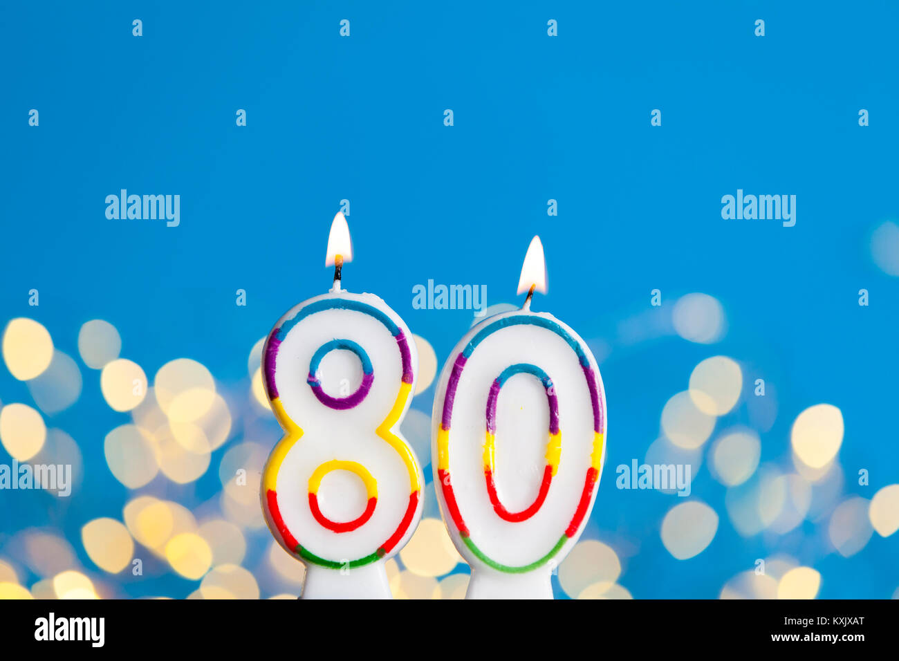 Number 80 birthday celebration candle against a bright lights and blue ...