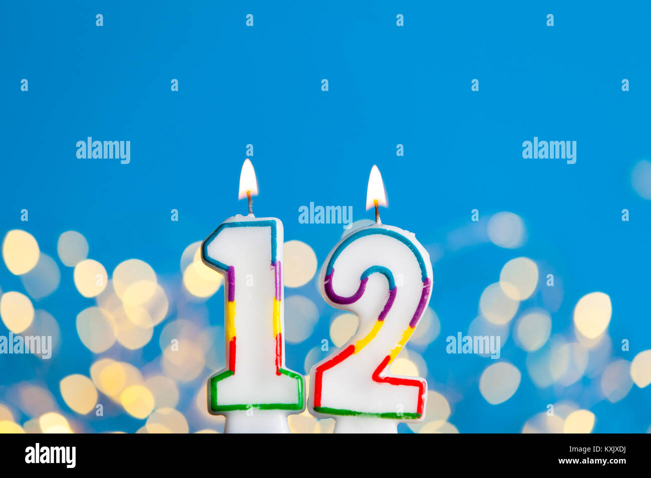 Number 12 birthday celebration candle against a bright lights and blue ...