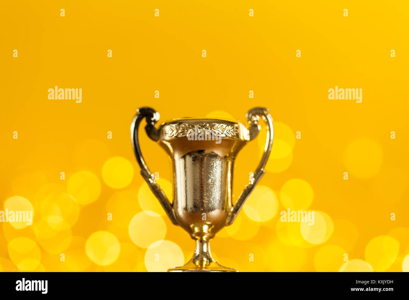 Gold award trophy against bright yellow background with blurred lights ...
