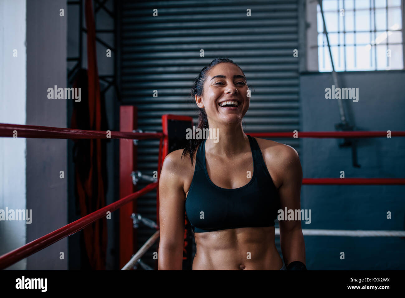 Smiling female boxer sitting in one corner of a boxing ring during her ...