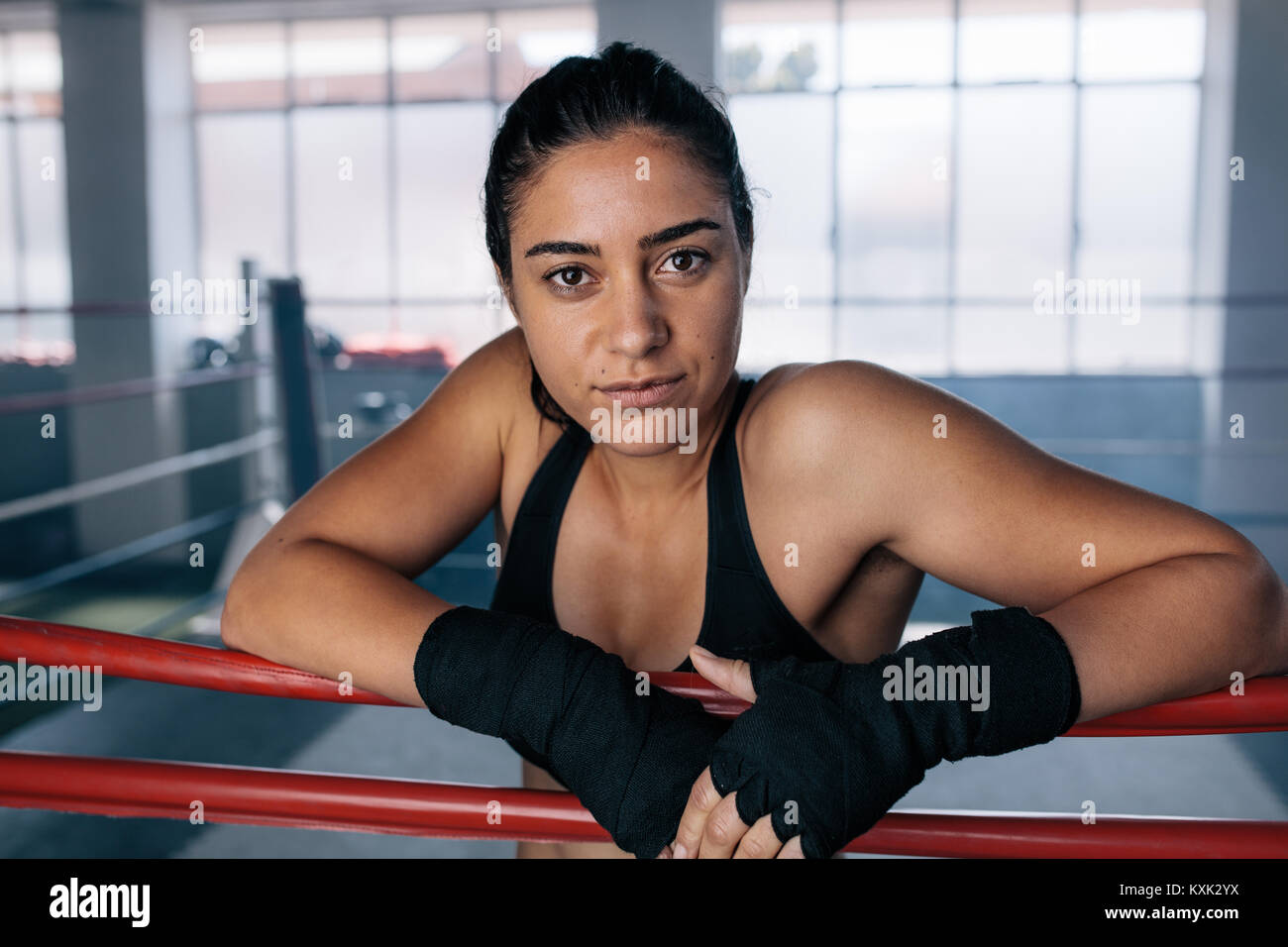 Female boxer standing inside a boxing ring. Boxer resting her arms on ...