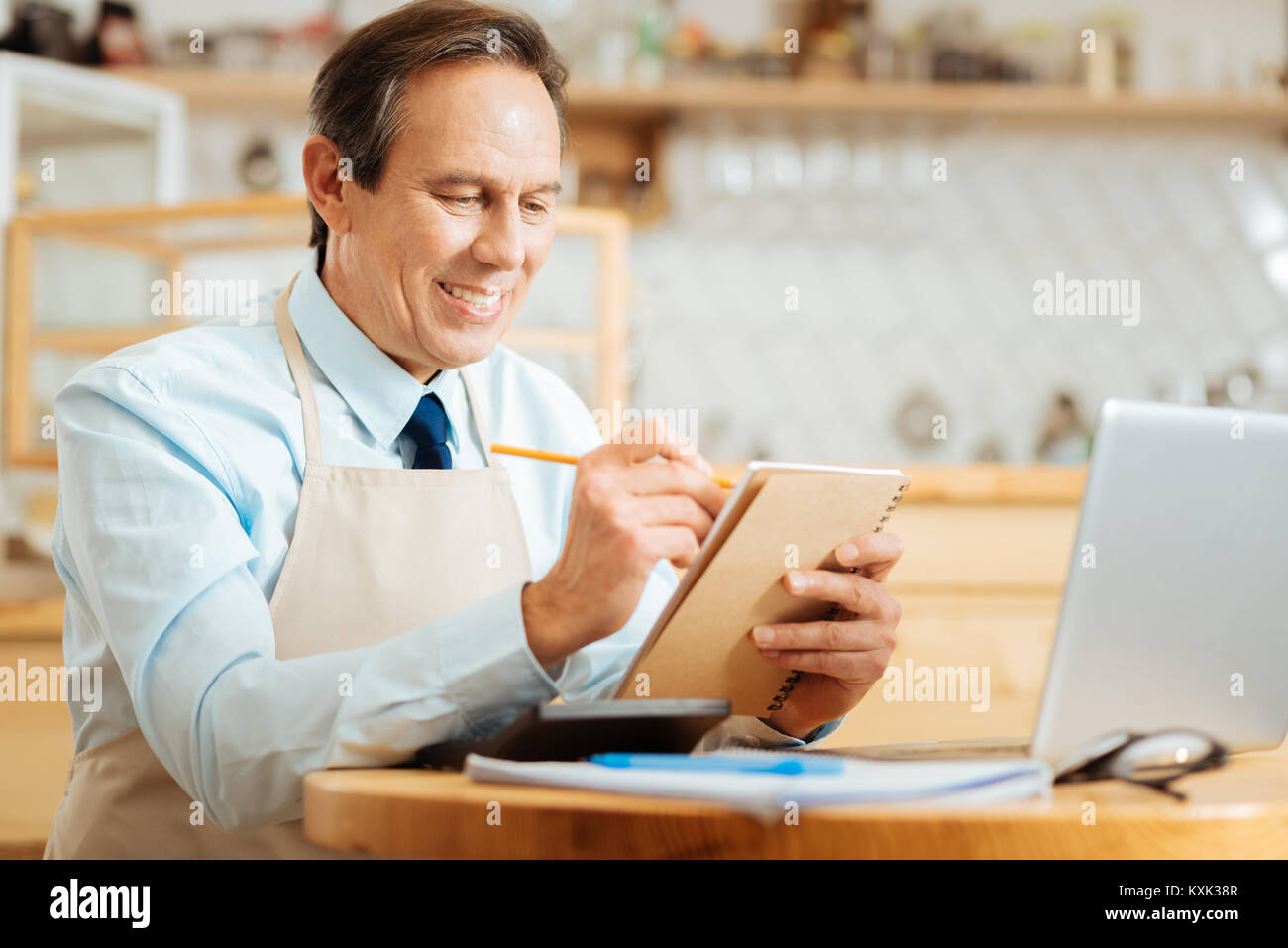 Pleasant clever man smiling and writing in his notebook Stock Photo - Alamy