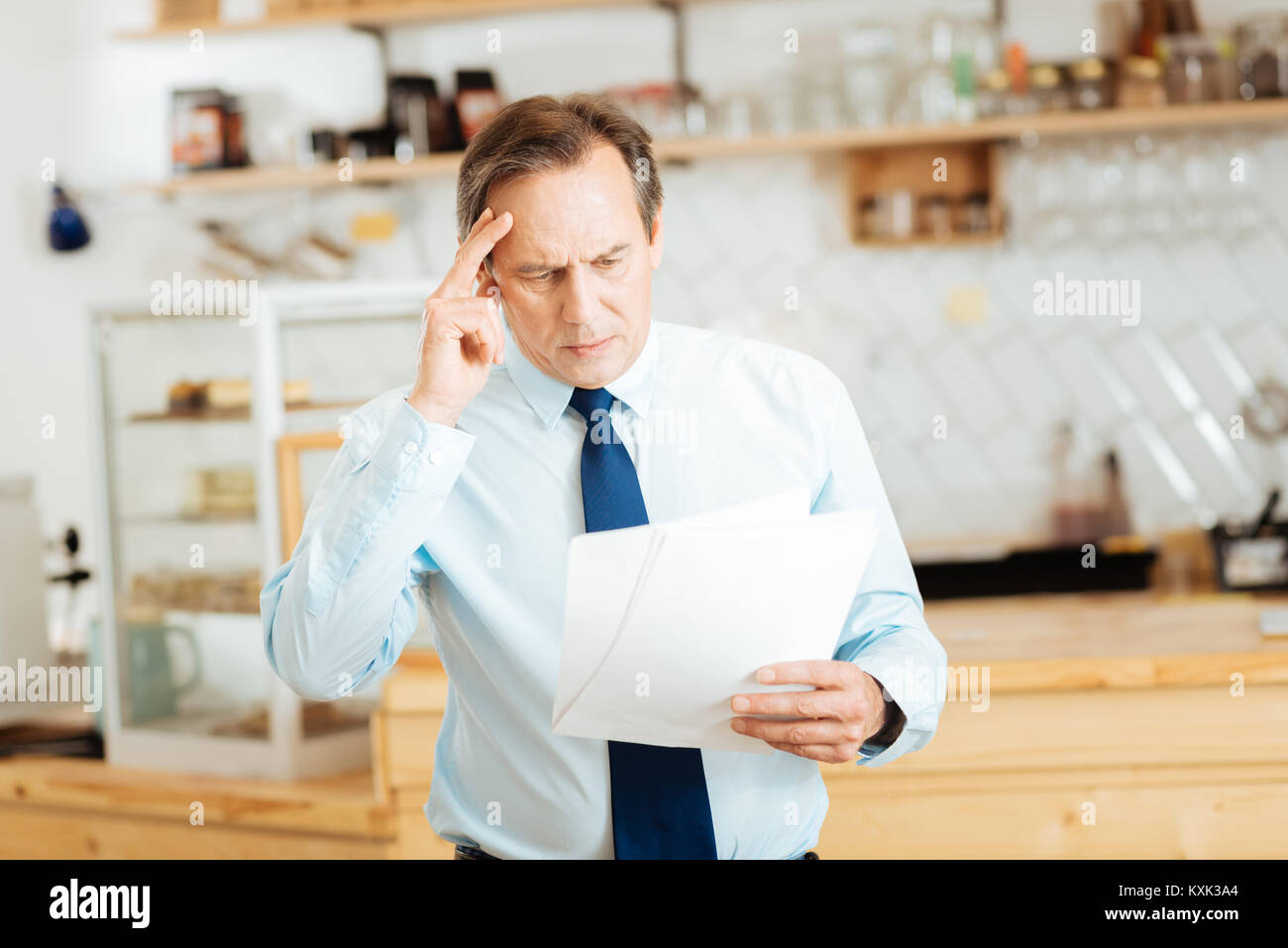 Thoughtful busy man overlooking documents and holding hand near head ...