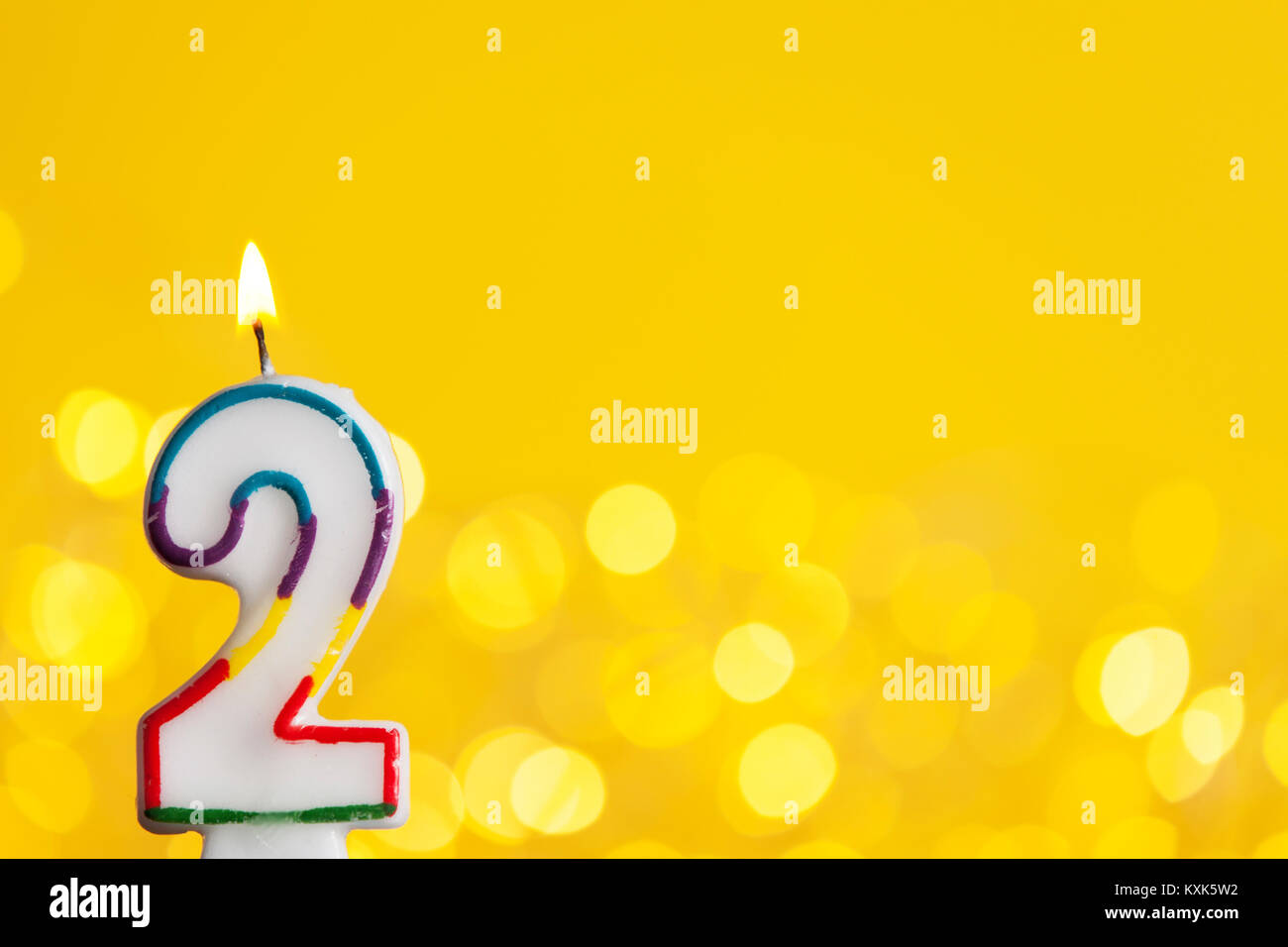 Number 2 birthday celebration candle against a bright lights and yellow ...