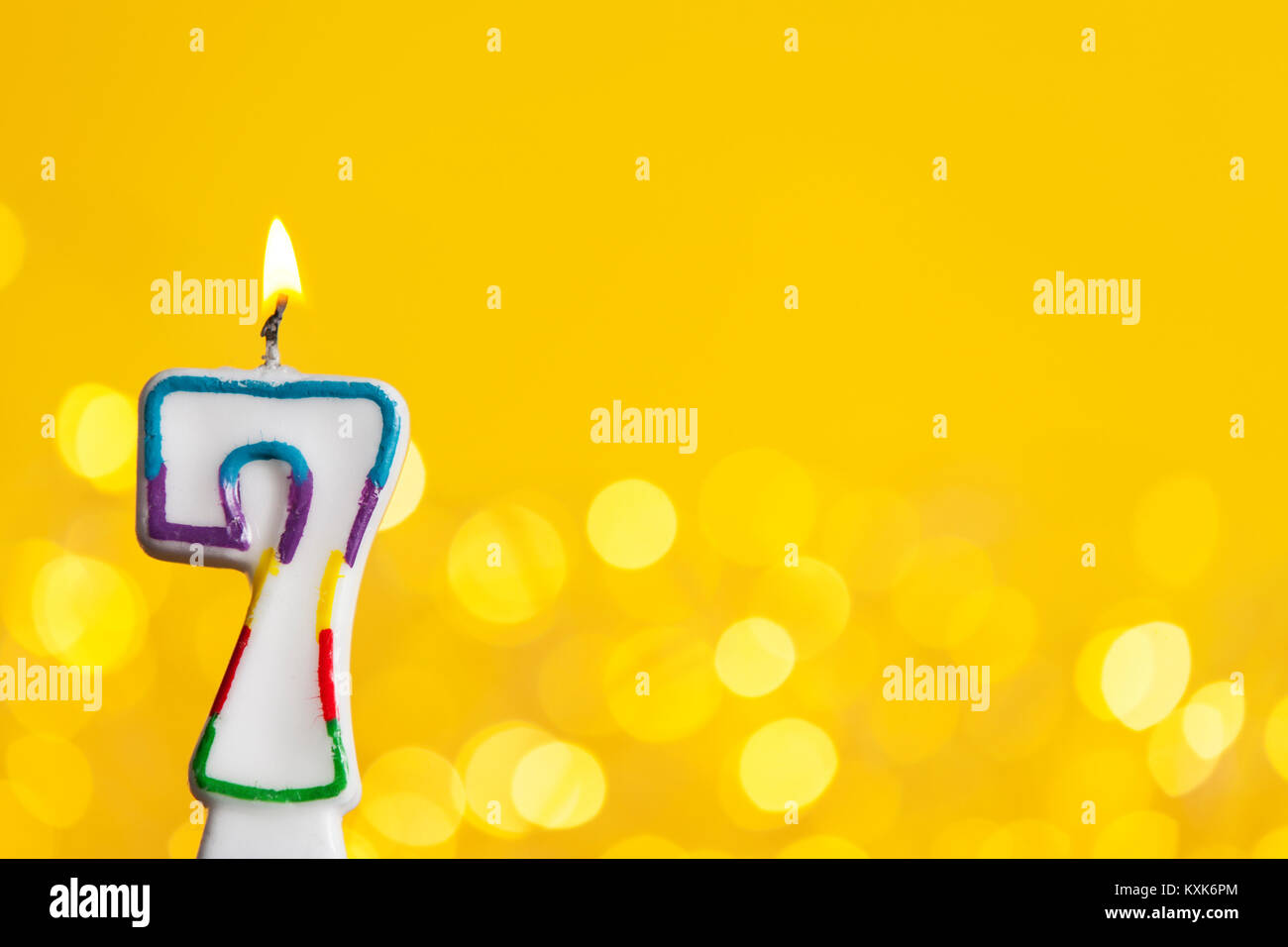 Number 7 birthday celebration candle against a bright lights and yellow ...