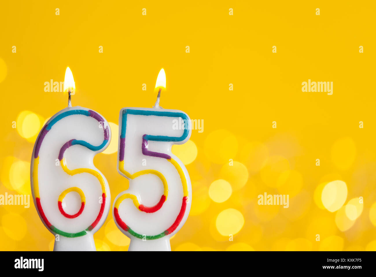 Number 65 birthday celebration candle against a bright lights and ...