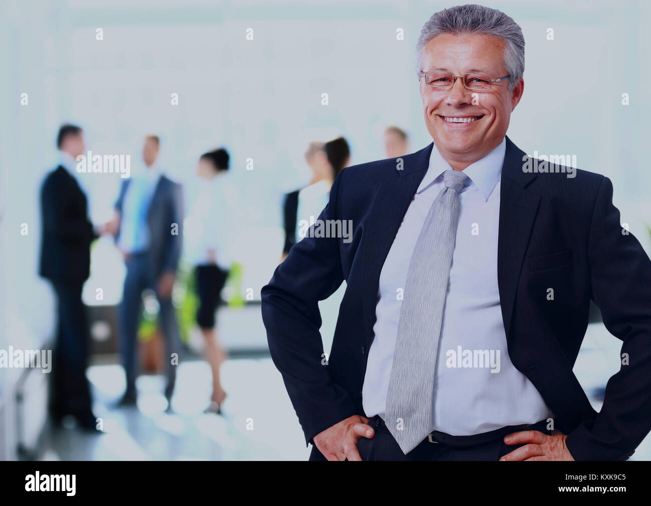 Successful business man standing with his staff in background at office ...