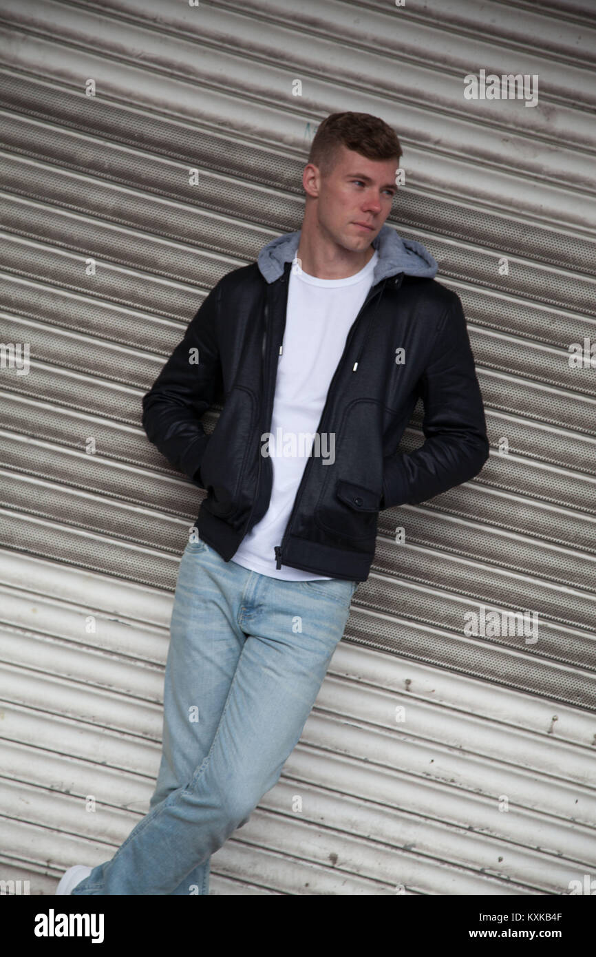 Good looking, blonde male model leaning on shop shutters in deserted ...
