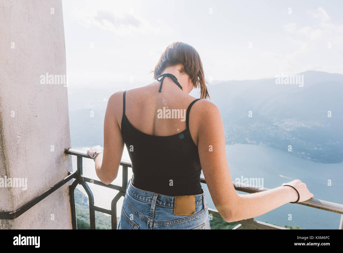 Rear view of young woman on viewing platform looking down at Lake Como ...