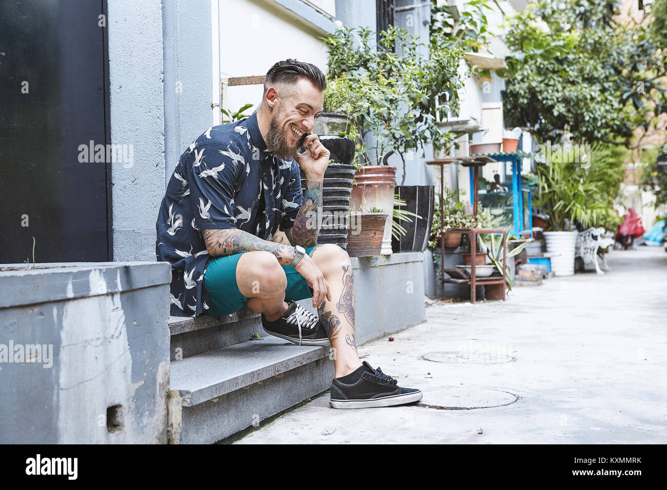 Young man sitting on doorstep in residential alleyway making smartphone ...