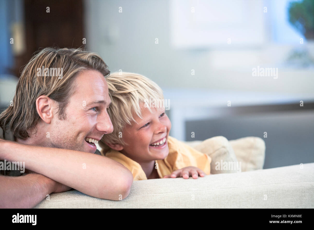 Father and son relaxing on sofa,looking away smiling Stock Photo - Alamy