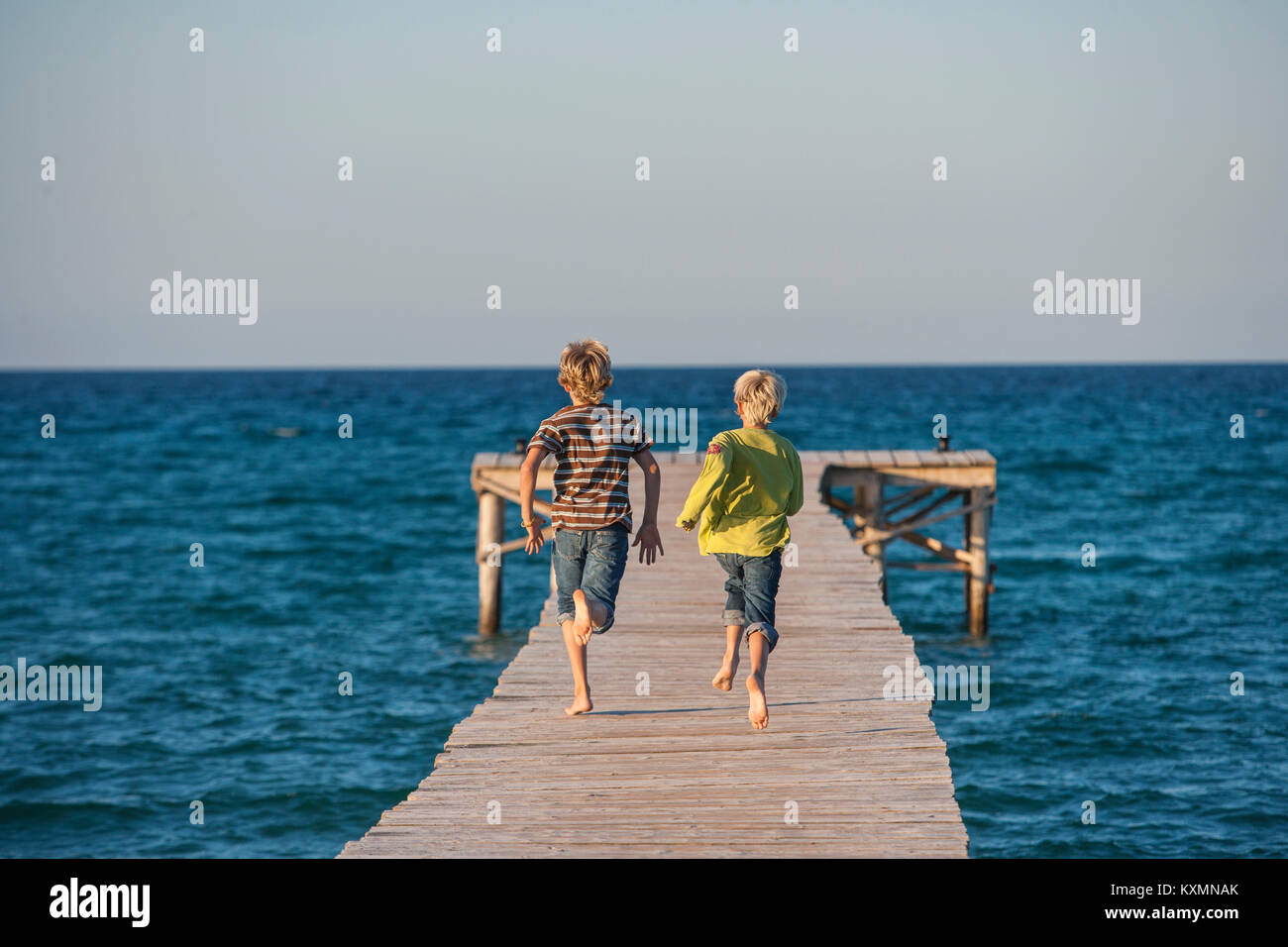Rear view of boys running on pier Stock Photo - Alamy