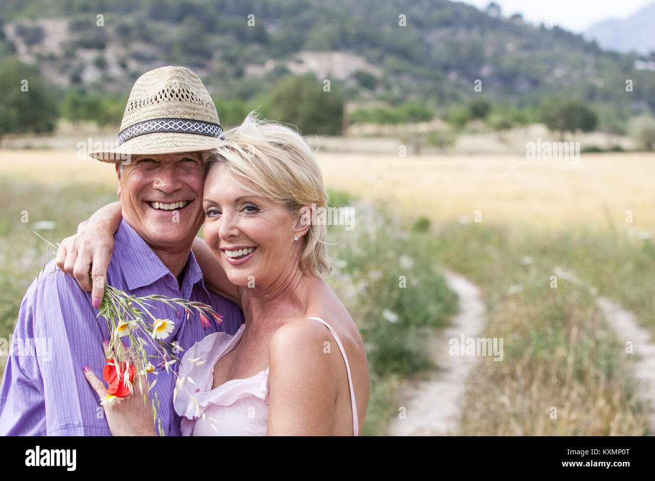 Couple in field with bunch of flowers hugging,looking at camera smiling ...