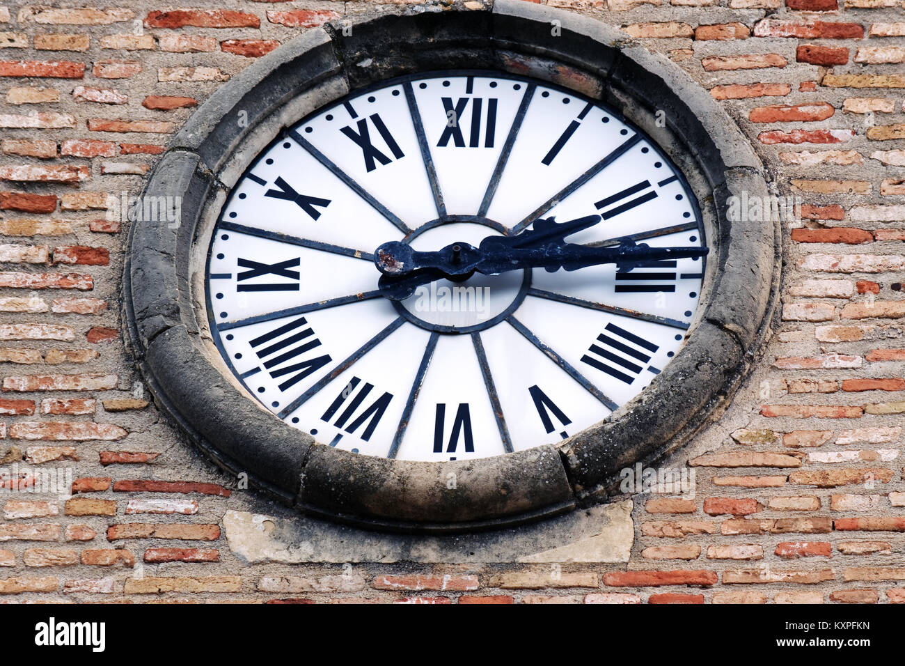 Old weathered clock with roman numerals and black iron hands surraunded ...
