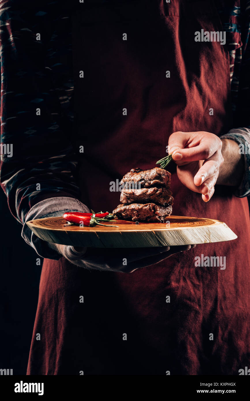 cropped shot of chef in apron holding wooden board with delicious ...