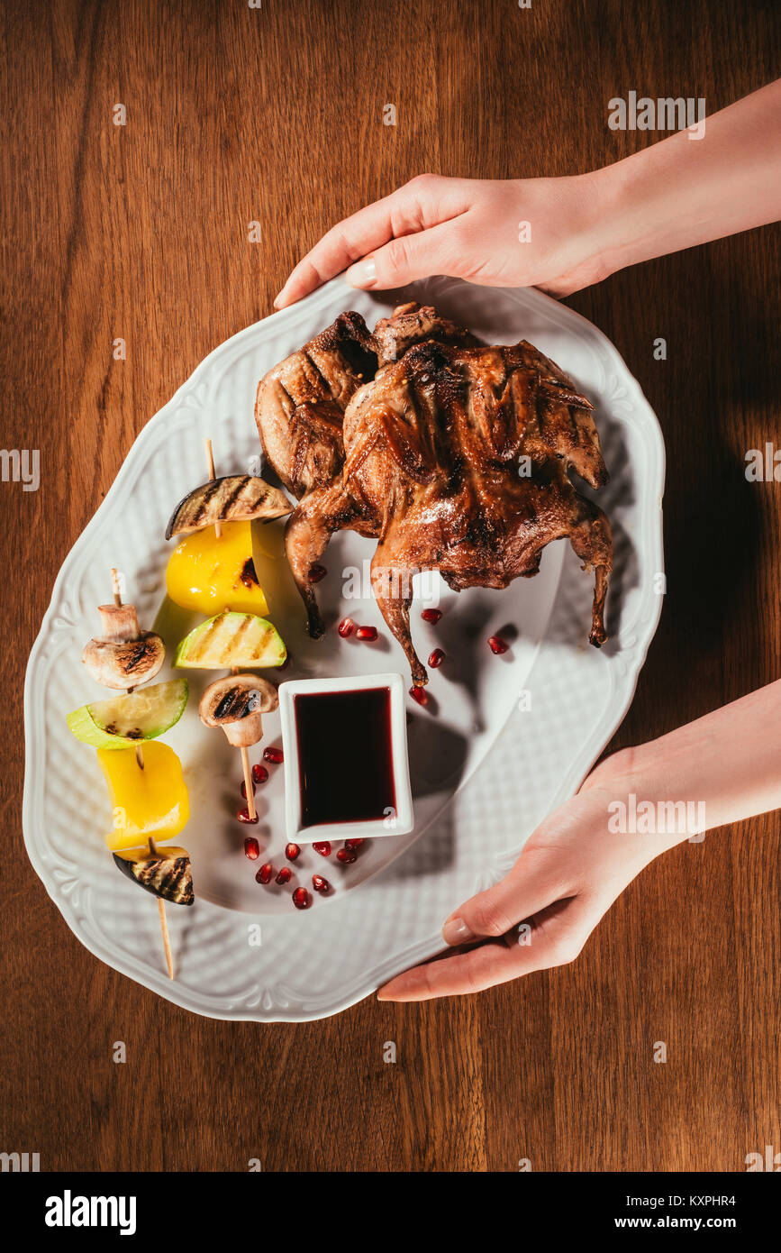 cropped image of hands holding palte with fried poultry and vegetables ...