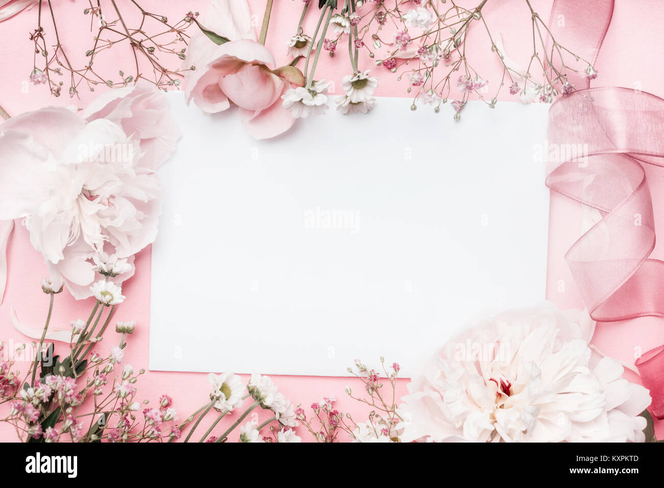 White blank card with pastel flowers and ribbon on pink pale background ...