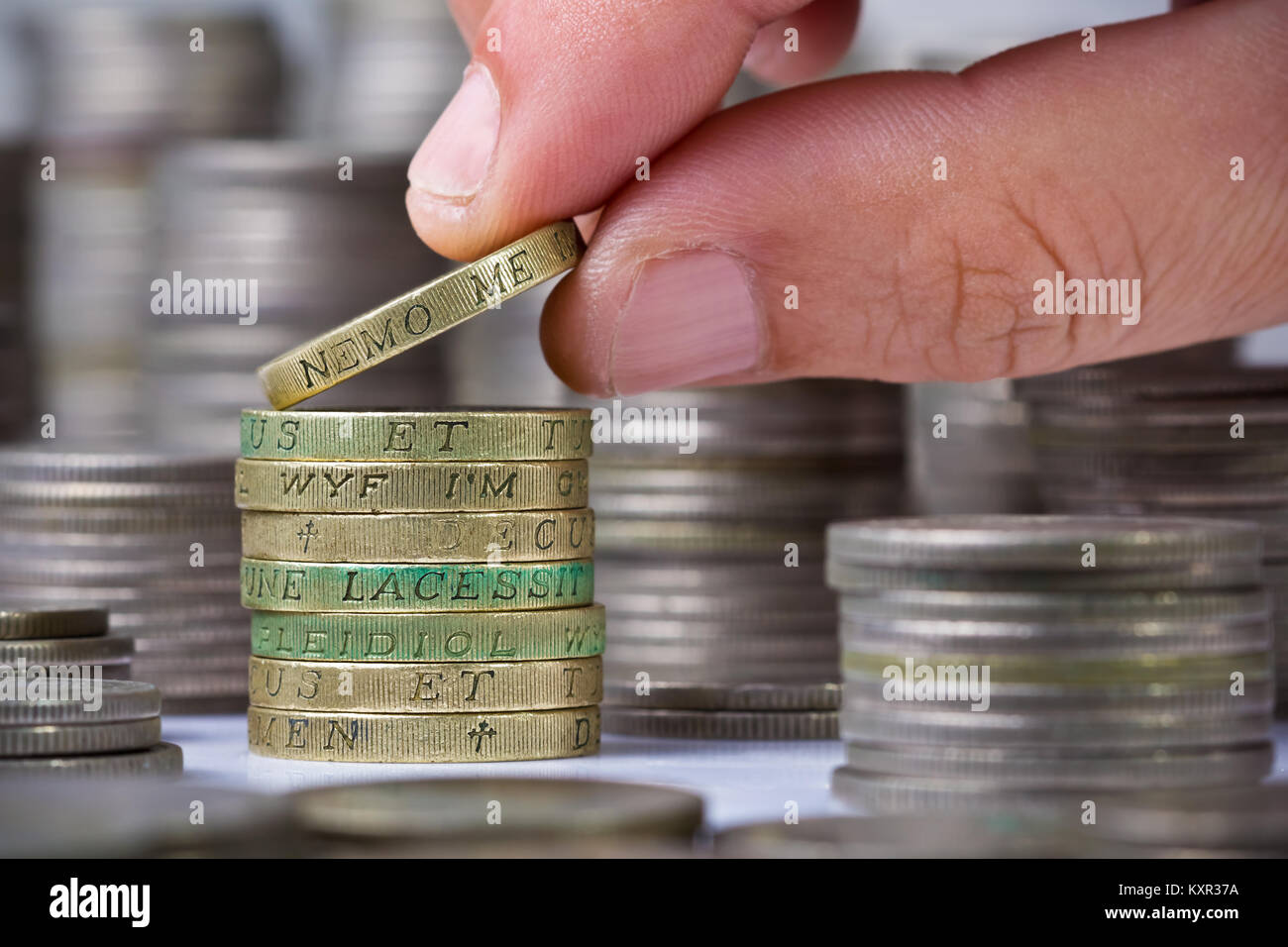 Closeup of a hand places a coin onto a british pound coins stack Stock ...