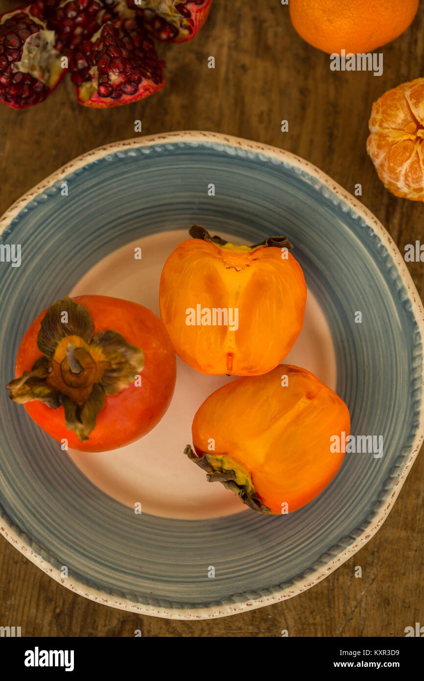 One persimmon sliced in half and one full persimmon in a white and blue ...
