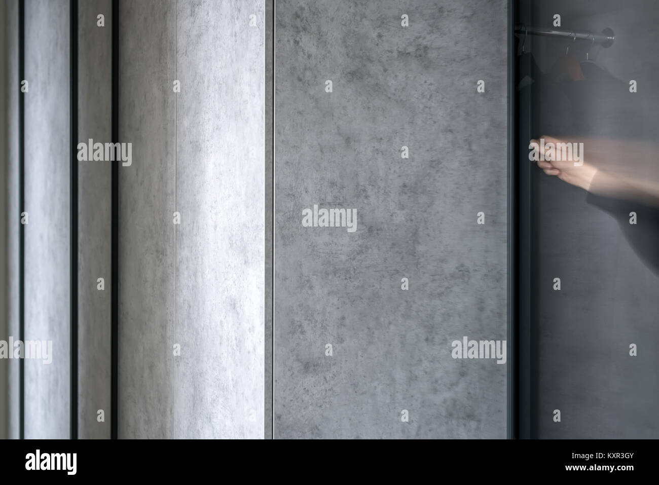 Opened textured gray wardrobe with hanging clothes. Hand is holding the ...