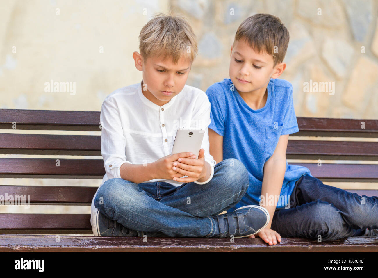 Boys with mobile phone sitting on the bench outdoors Stock Photo - Alamy