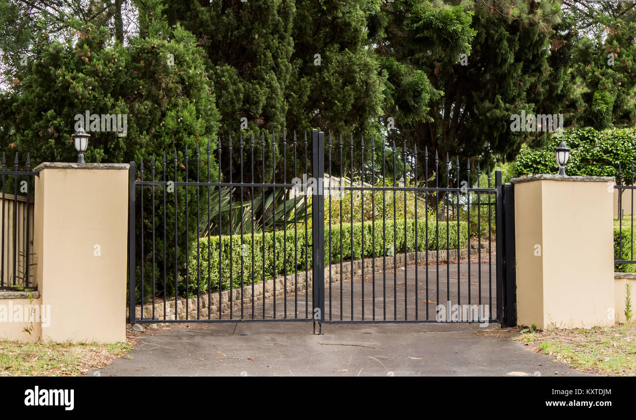 Metal driveway entrance gates set in brick fence with garden trees in ...