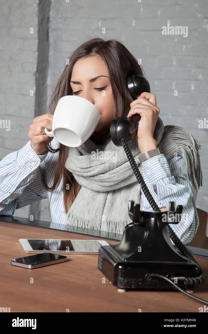 A sick business woman is drinking hot tea and talking on the phone ...