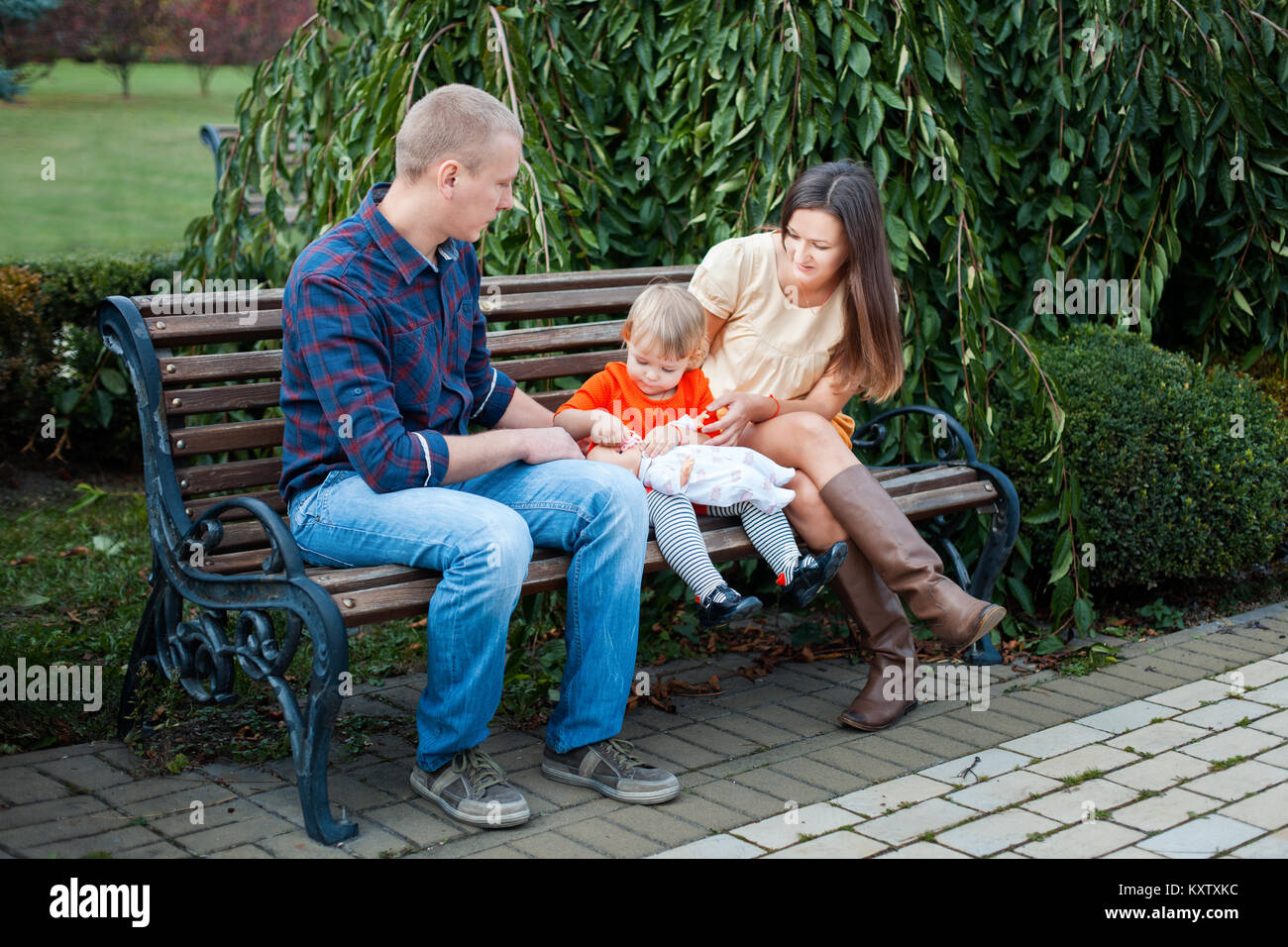 Young family sitting on a bench in the park Stock Photo - Alamy