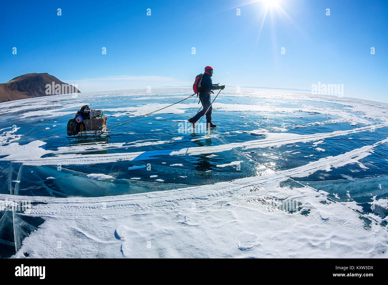 man with a sledge and trekking pole is on the ice of Lake Baikal Stock ...