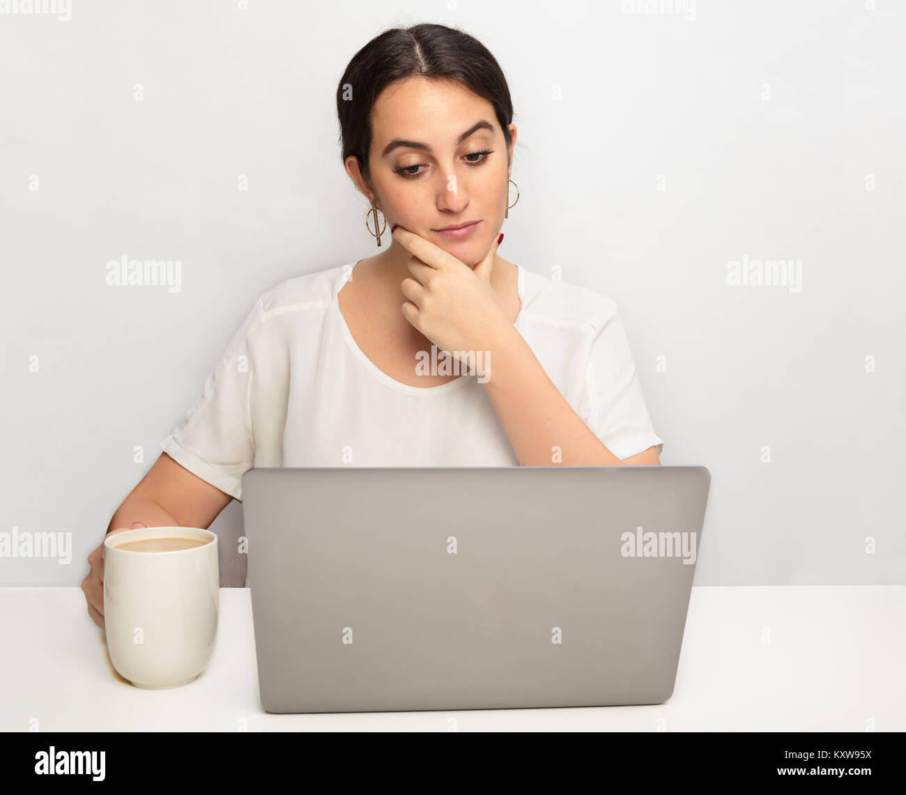 Thoughtful young woman working on a laptop computer looking at the ...