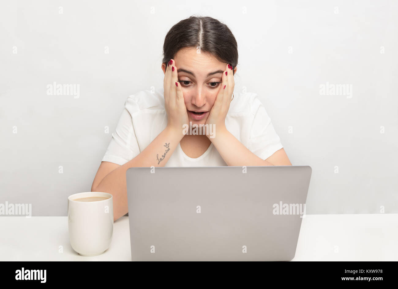 Young woman staring at a laptop in disbelief and shock resting her face ...